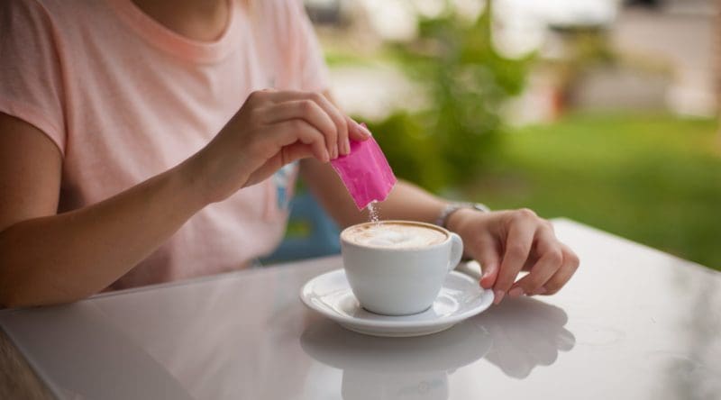 Woman hand pouring a sugar packet into a cup of coffee. | Cabot Health